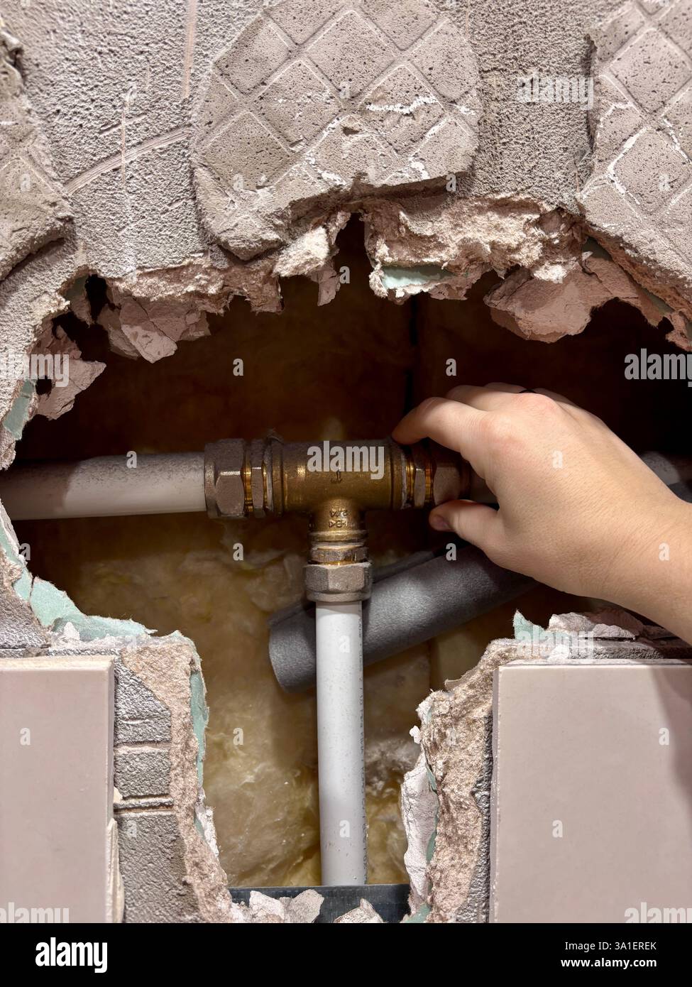 A persons hand touching a brass pipe fitting inside a damaged wall with ...