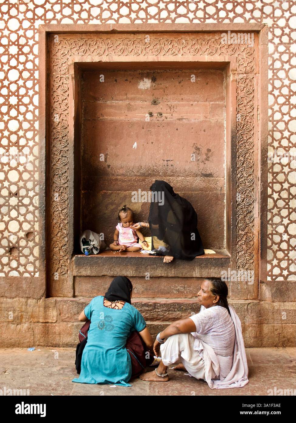 Women and a child rest in the carved stone recess of a Mughal-era wall ...