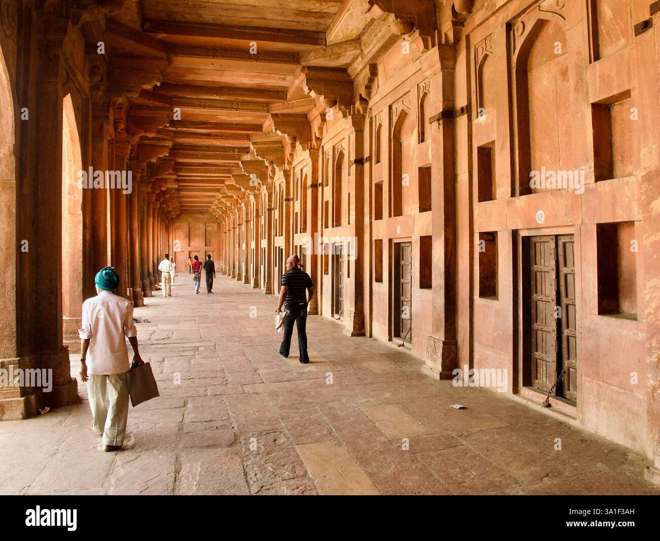 People walk through a colonnaded red sandstone corridor in the historic ...