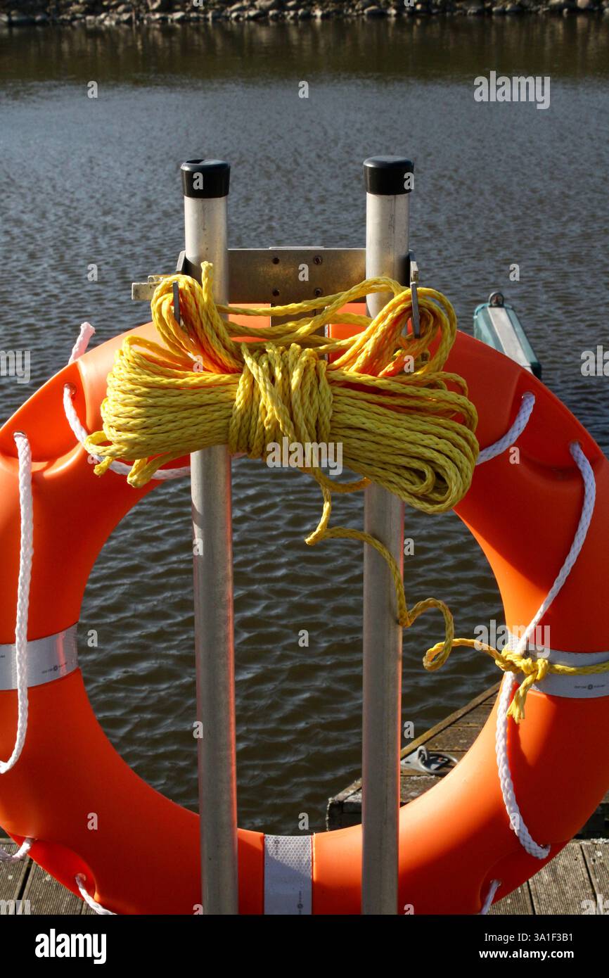 Lifesaver ring, bright orange, yellow rope, wooden dock, calm water ...