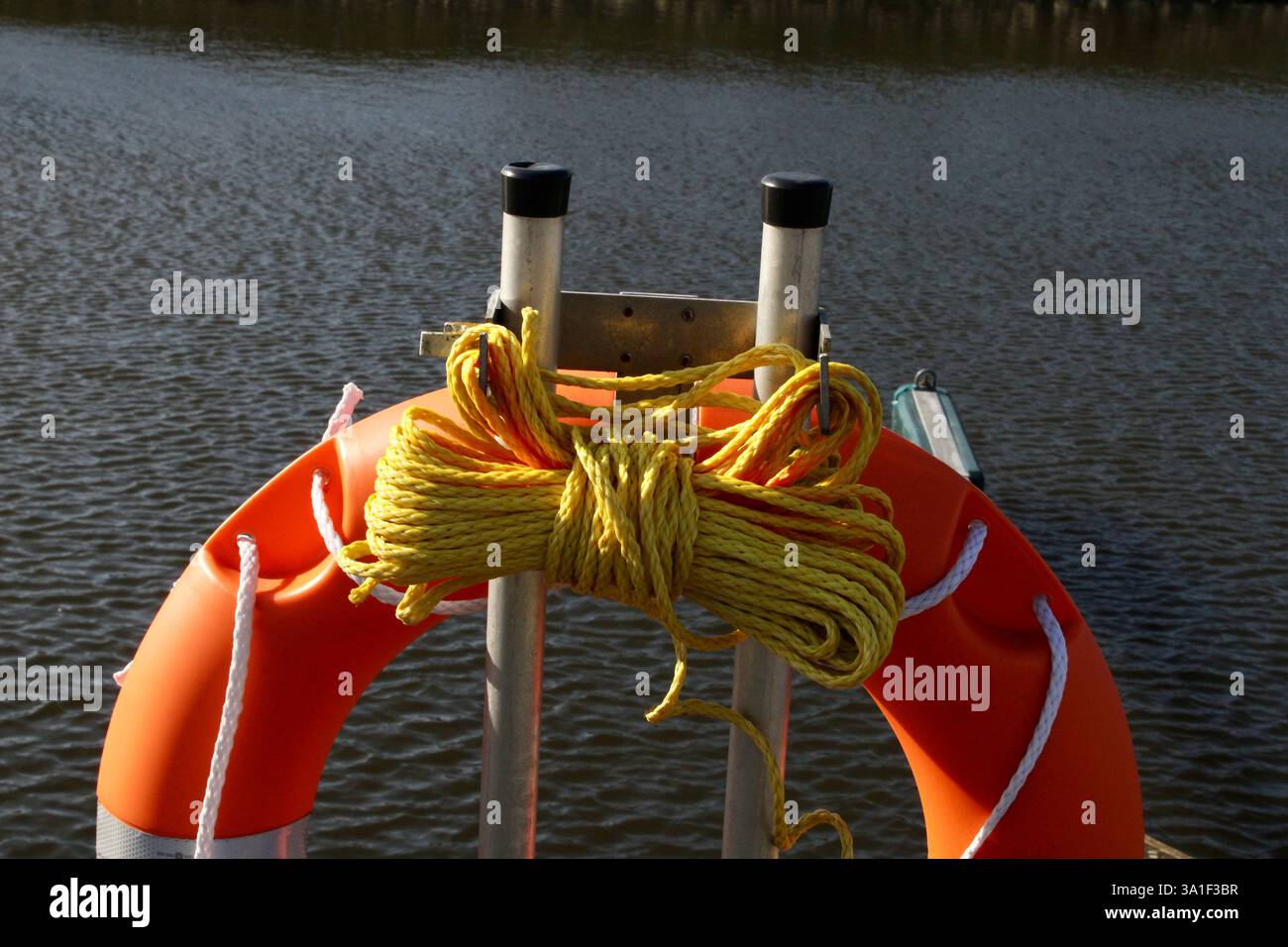 Lifesaver ring, bright orange, yellow rope, wooden dock, calm water ...