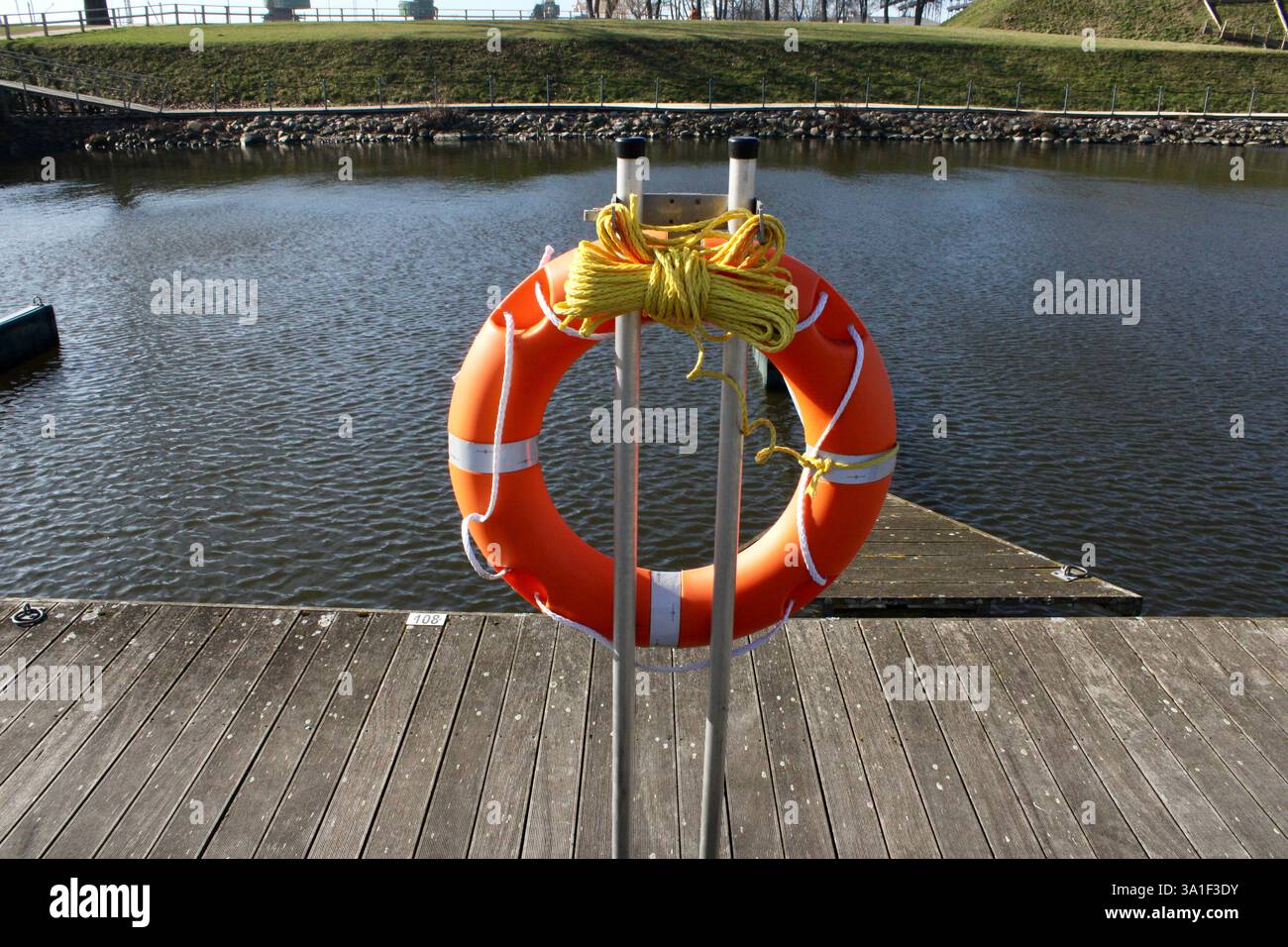 Lifesaver ring, bright orange, yellow rope, wooden dock, calm water ...