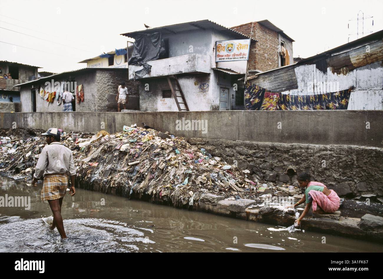 A woman washing cloth in dirty water along a canal dumped with garbage ...