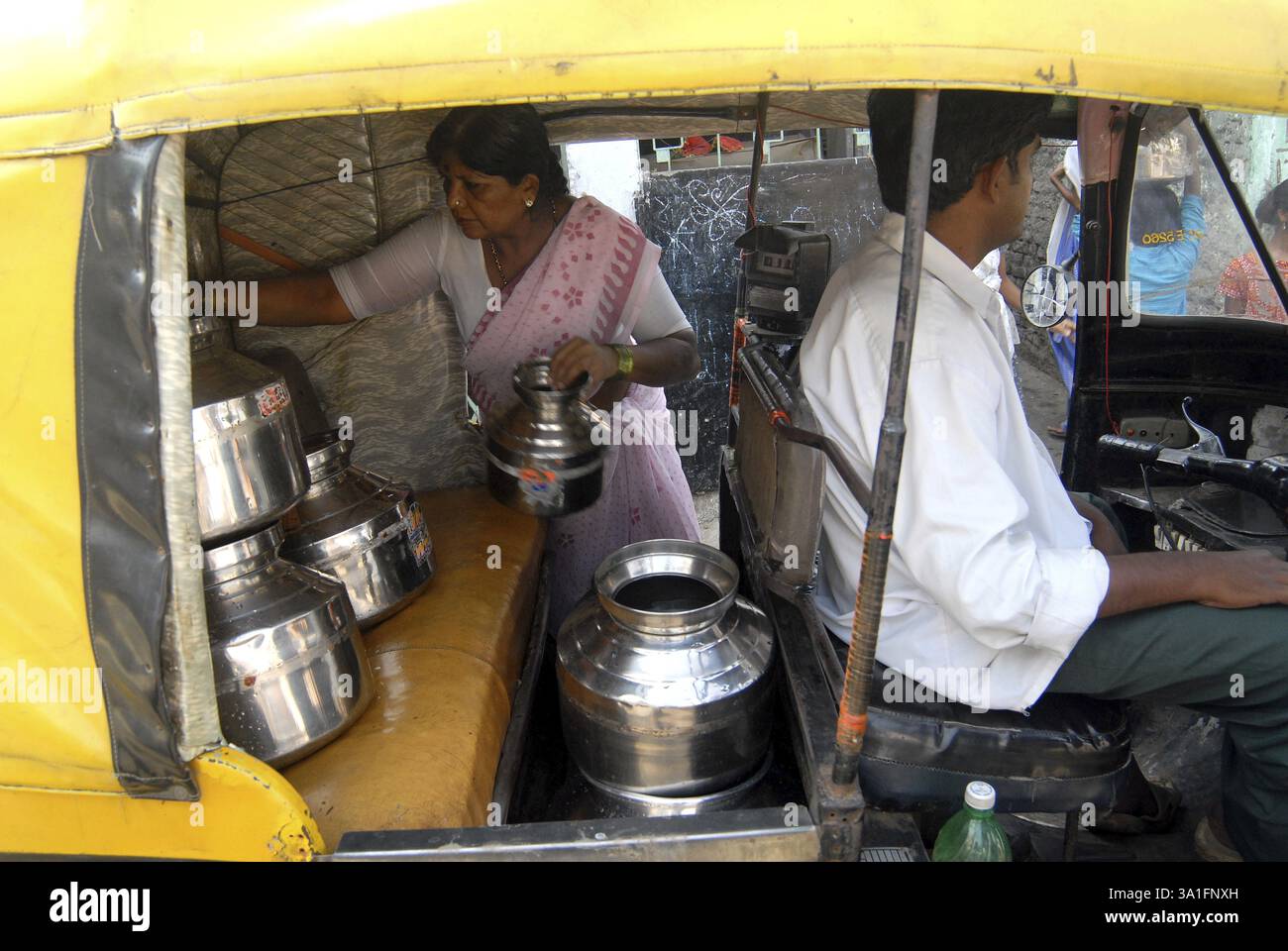 A woman fill drinking water in stainless steel containers in a rickshaw ...
