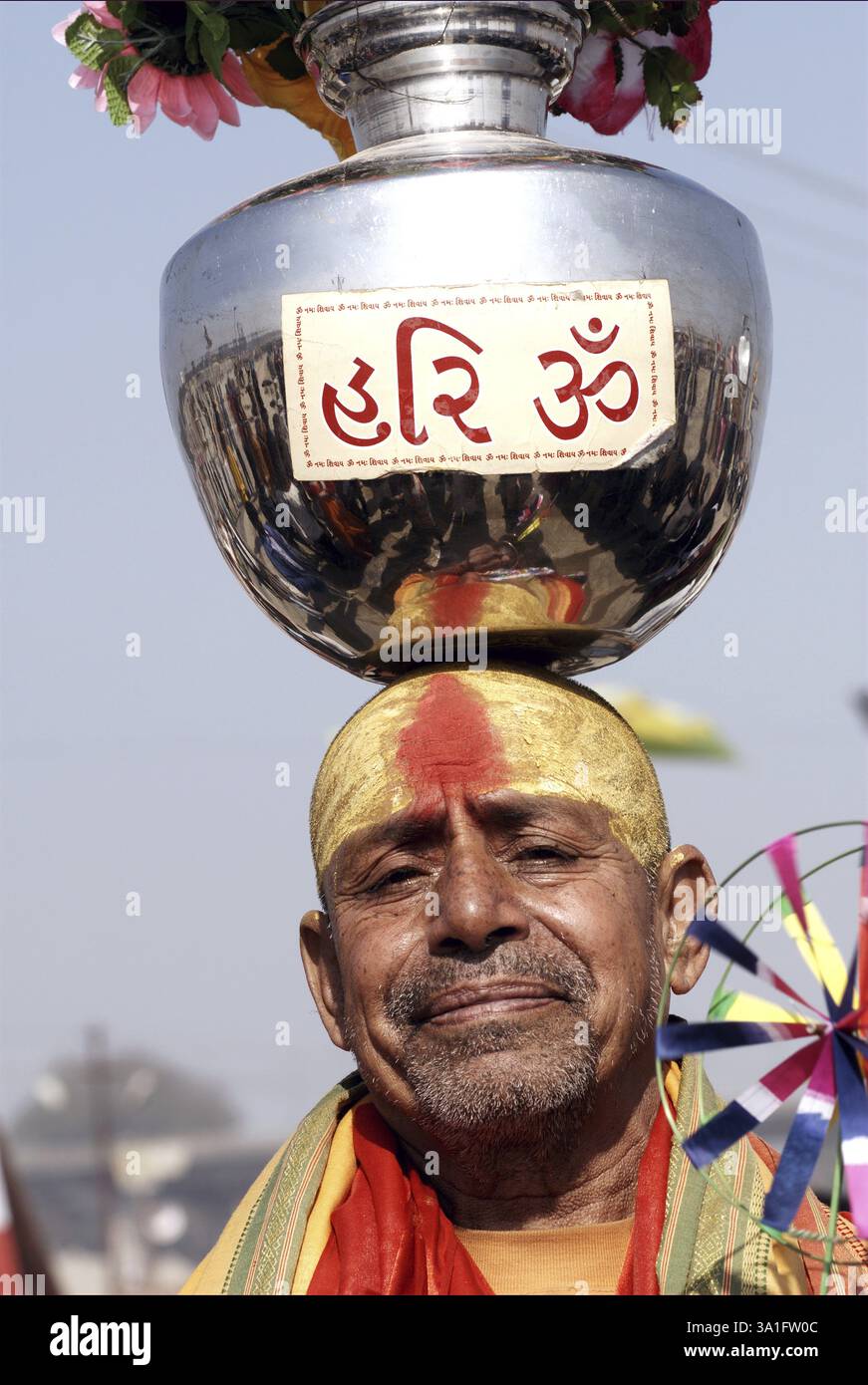 A saint, sadhu balance a stainless steel jar with flowers on his head ...