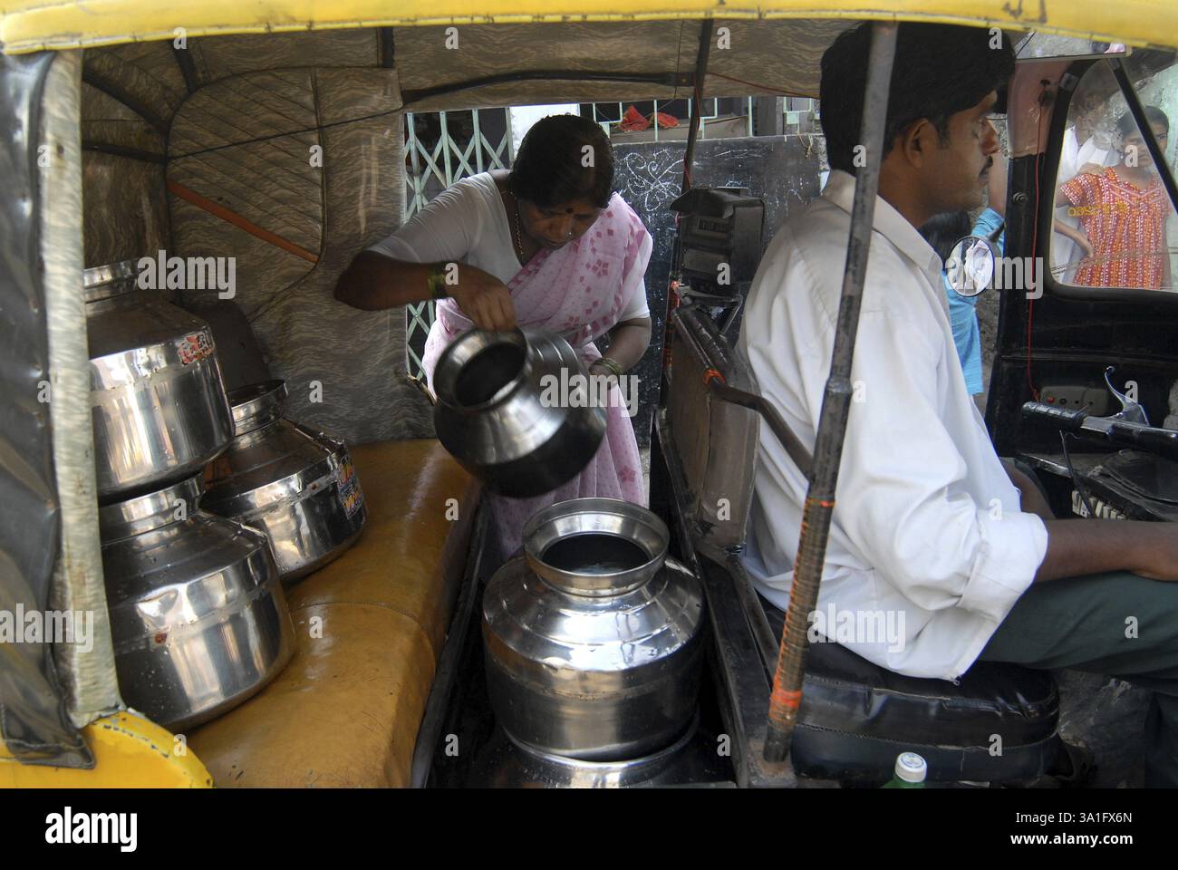 A woman fill drinking water in stainless steel containers in a rickshaw ...