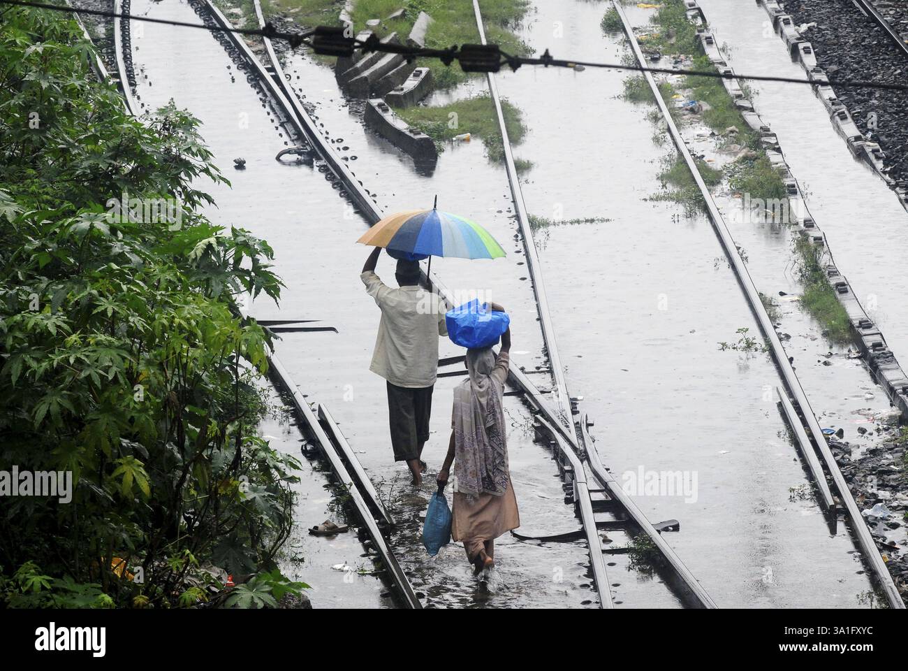 Commuters walk in the flooded waters on the railway tracks caused due to heavy rains at Kurla ...