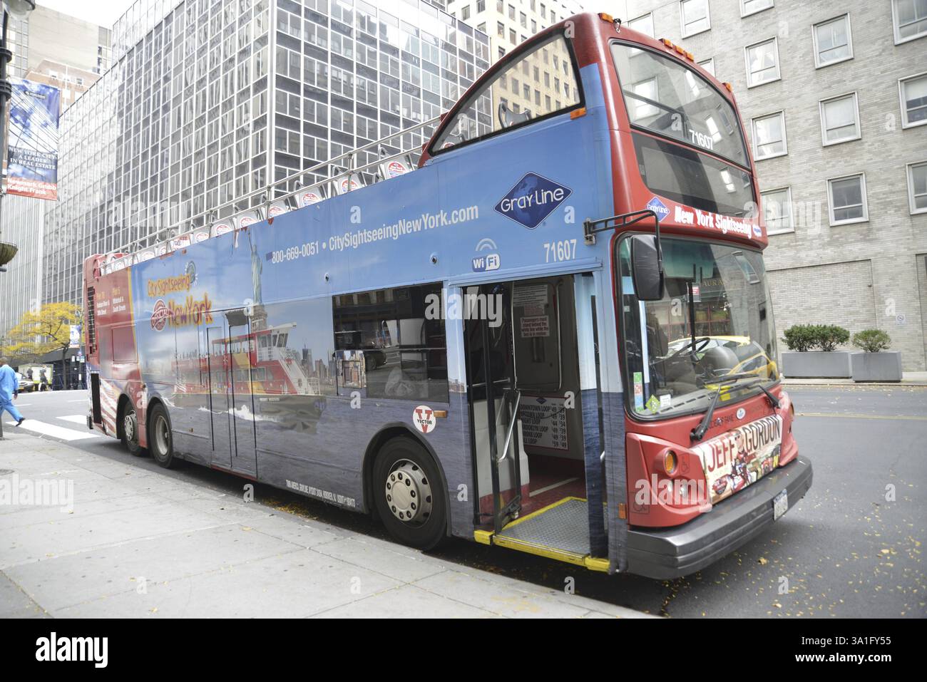 An open-top double-decker bus stands on a street corner in an urban ...