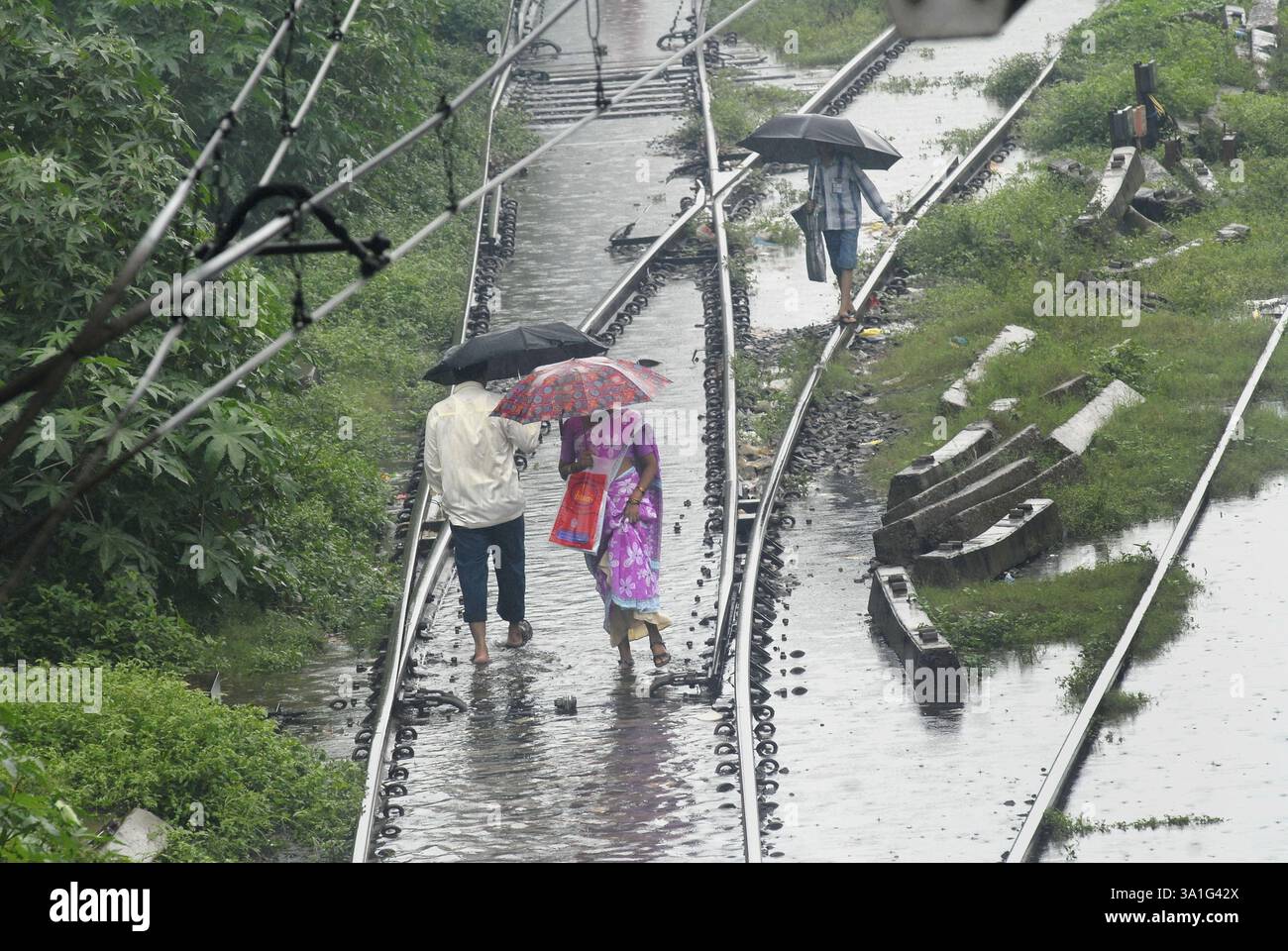 Commuters walk in the flooded waters on the railway tracks caused due to heavy rains at Kurla ...
