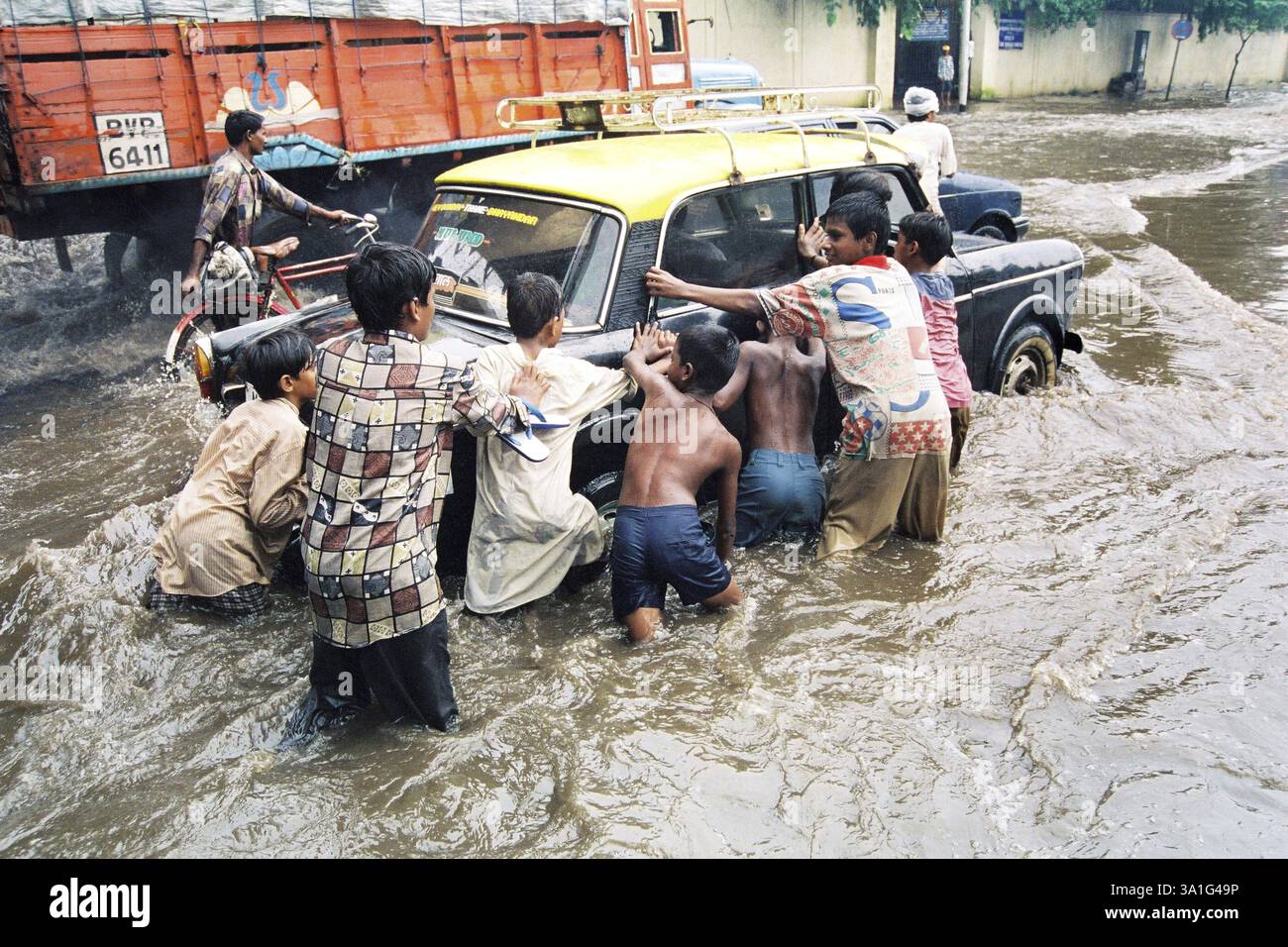 Street children push a taxi stranded in the flooded waters due to heavy ...
