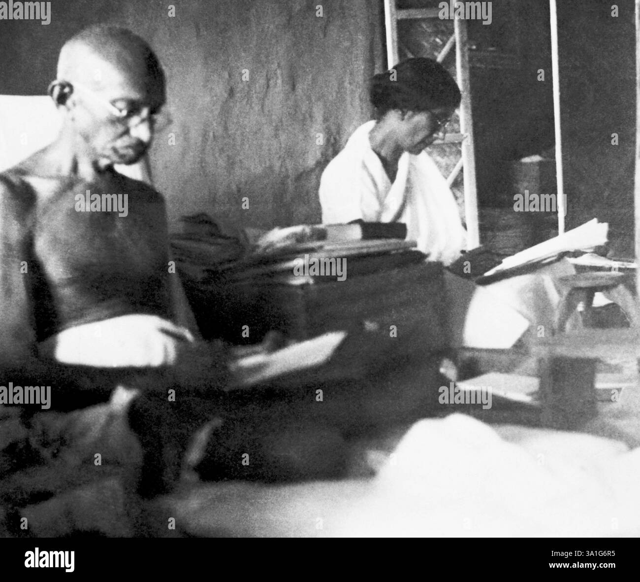 Mahatma Gandhi sitting in his hut at Sevagram Ashram, 1938, next to him ...