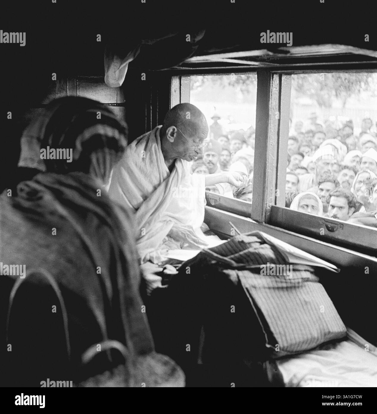 Mahatma Gandhi, sitting in a train compartment, writing with his right ...