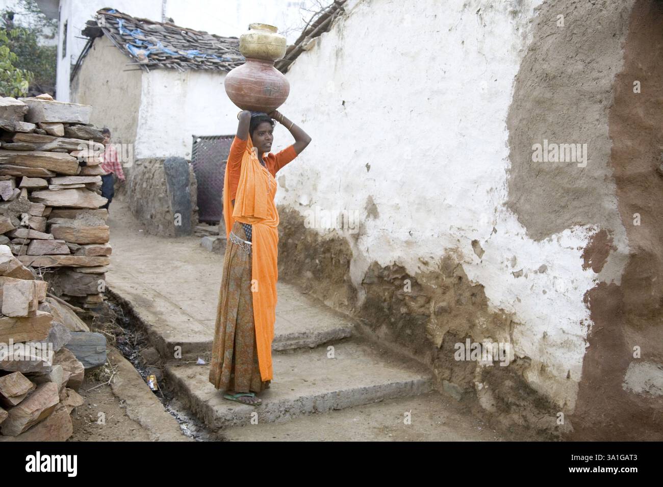 Rural woman carrying water in clay pot on her head standing in village ...
