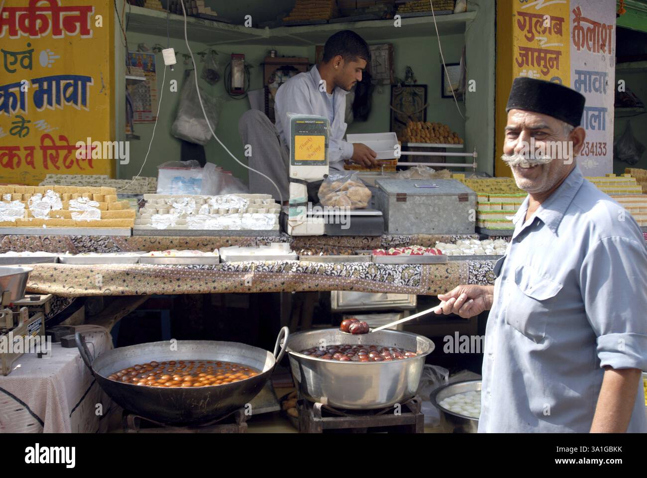 South Asian Indian sweet shop, owner of the shop showing sweets with ...