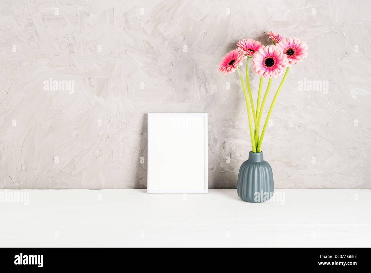 Pink gerbera flowers in a gray ceramic vase next to an empty white ...