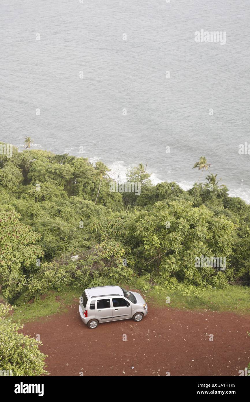 Car parked on red soil ground surrounded by greenery and sea, Goa ...