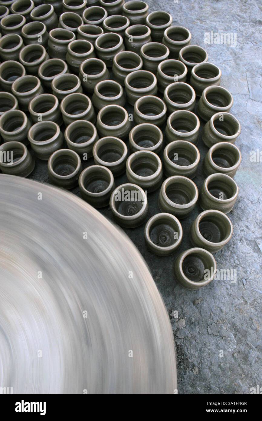 Potter's wooden wheel in motion and several freshly made earthen pots ...