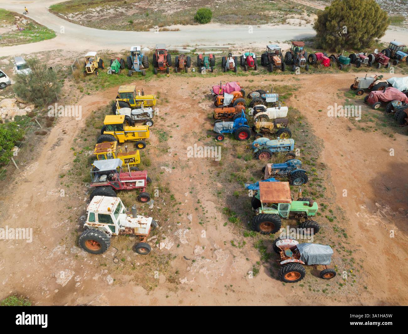 Aerial view of old rusting tractors lined up in a coastal paddock at ...
