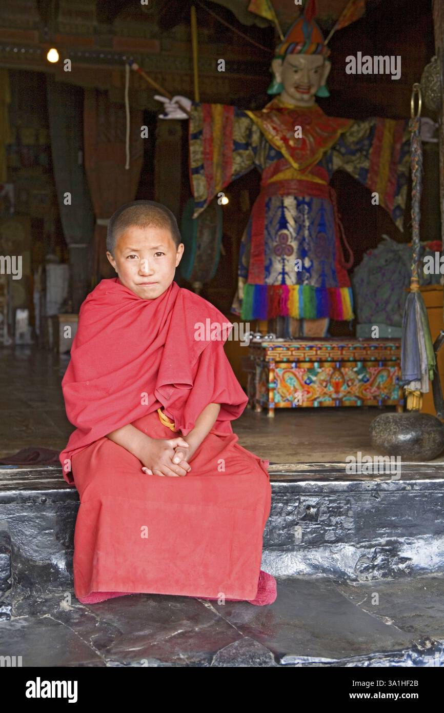 A young lama in his red robes seating outside the temple gate of the ...