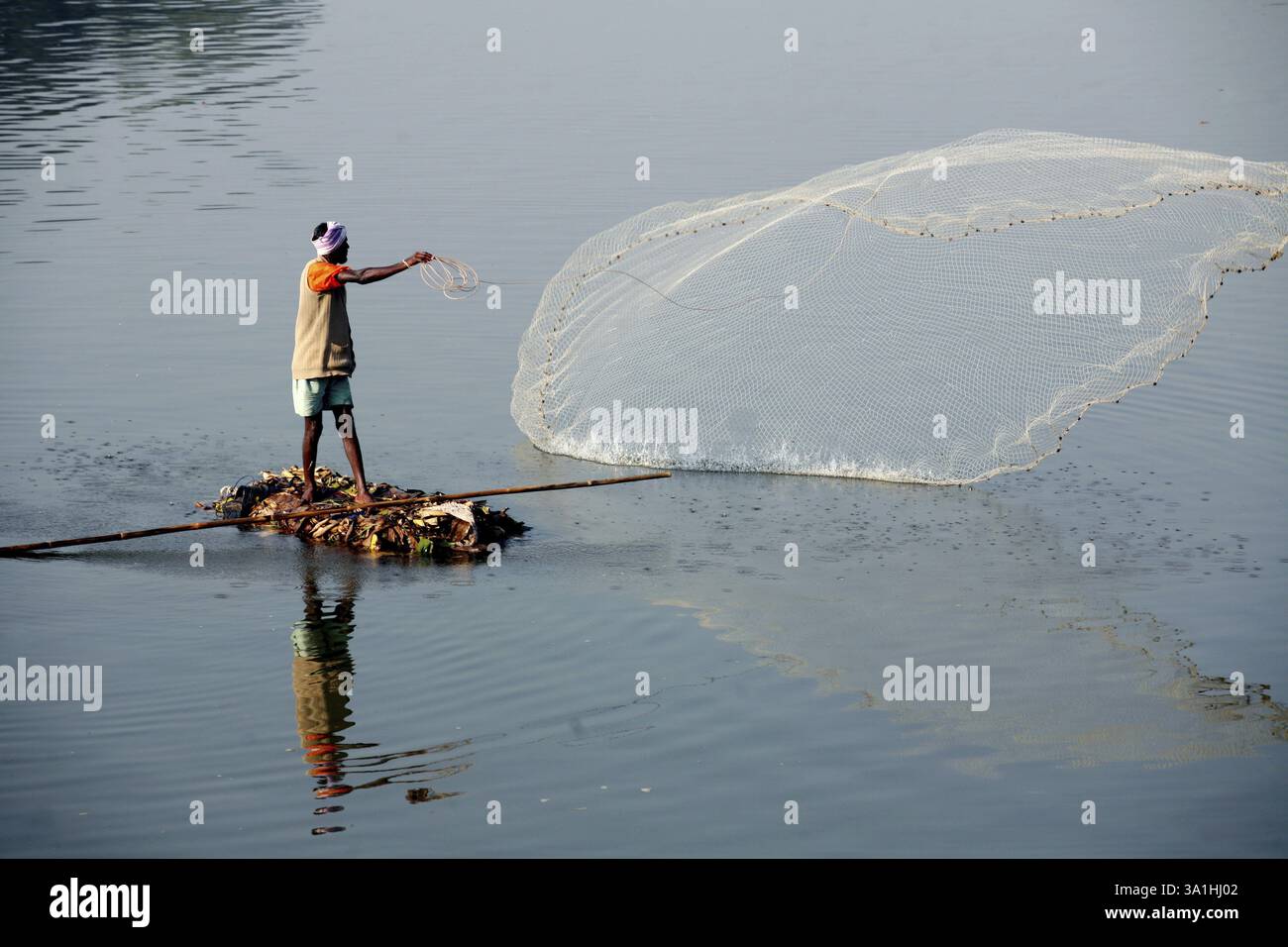 A fisherman from the Haripur village on a makeshift boat throwing his ...