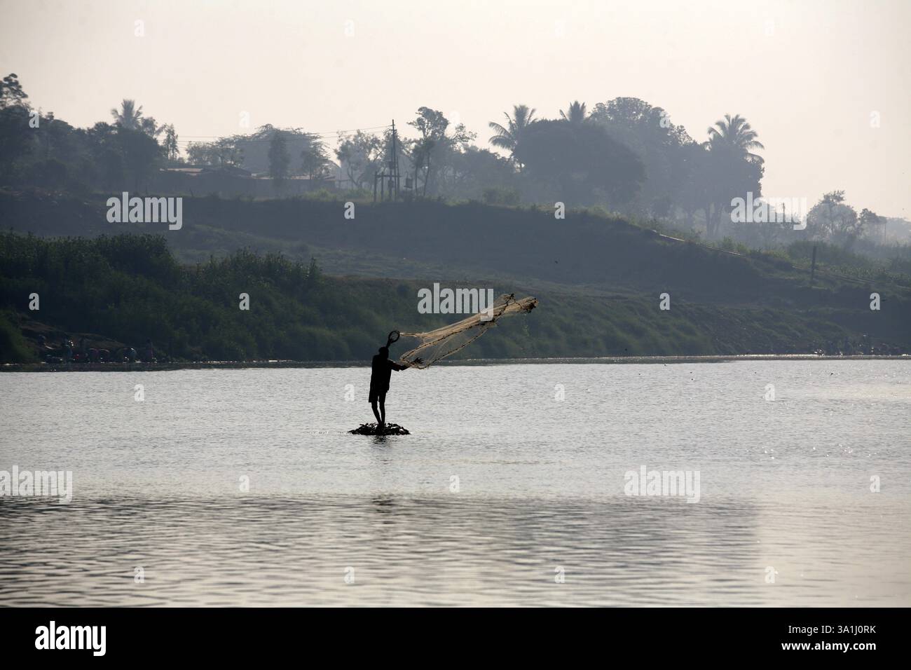 A fisherman from the Haripur village on a makeshift boat throwing his ...