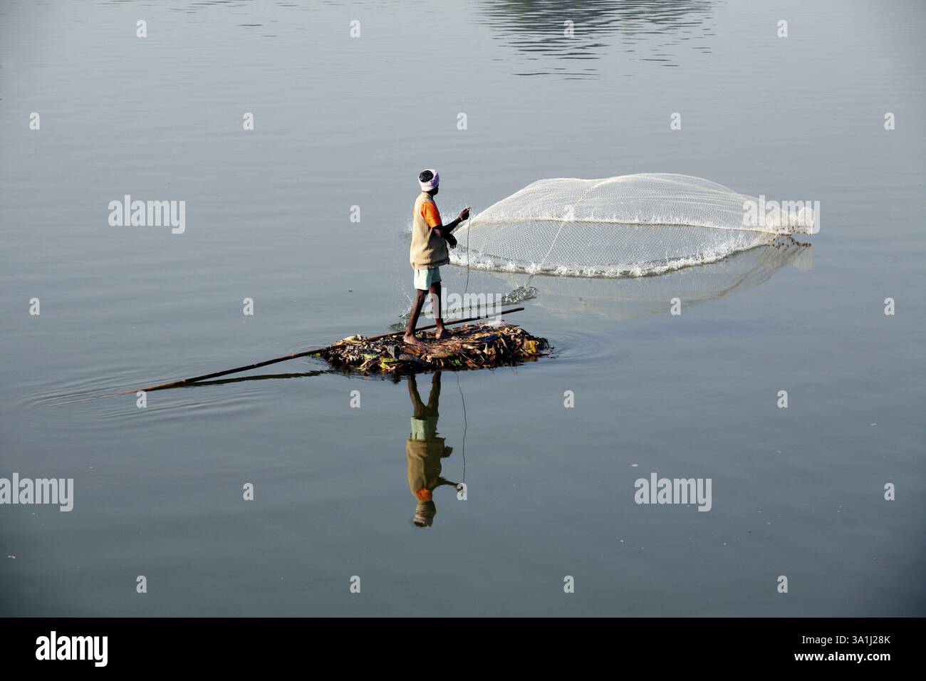 A fisherman from the Haripur village on a makeshift boat throwing his ...