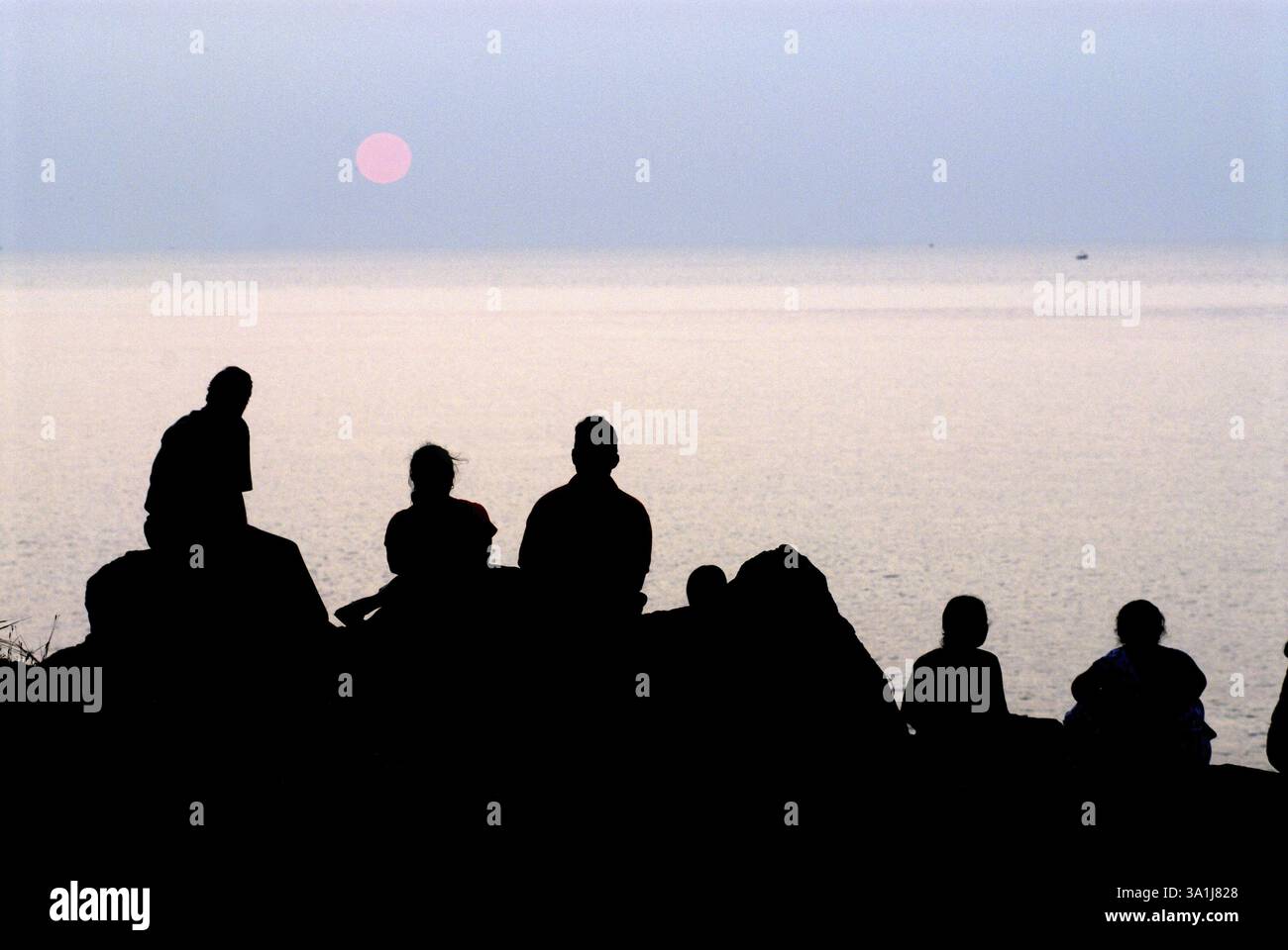 Tourists sitting on rocks and watching Sunset at Harihareshwar Beach ...