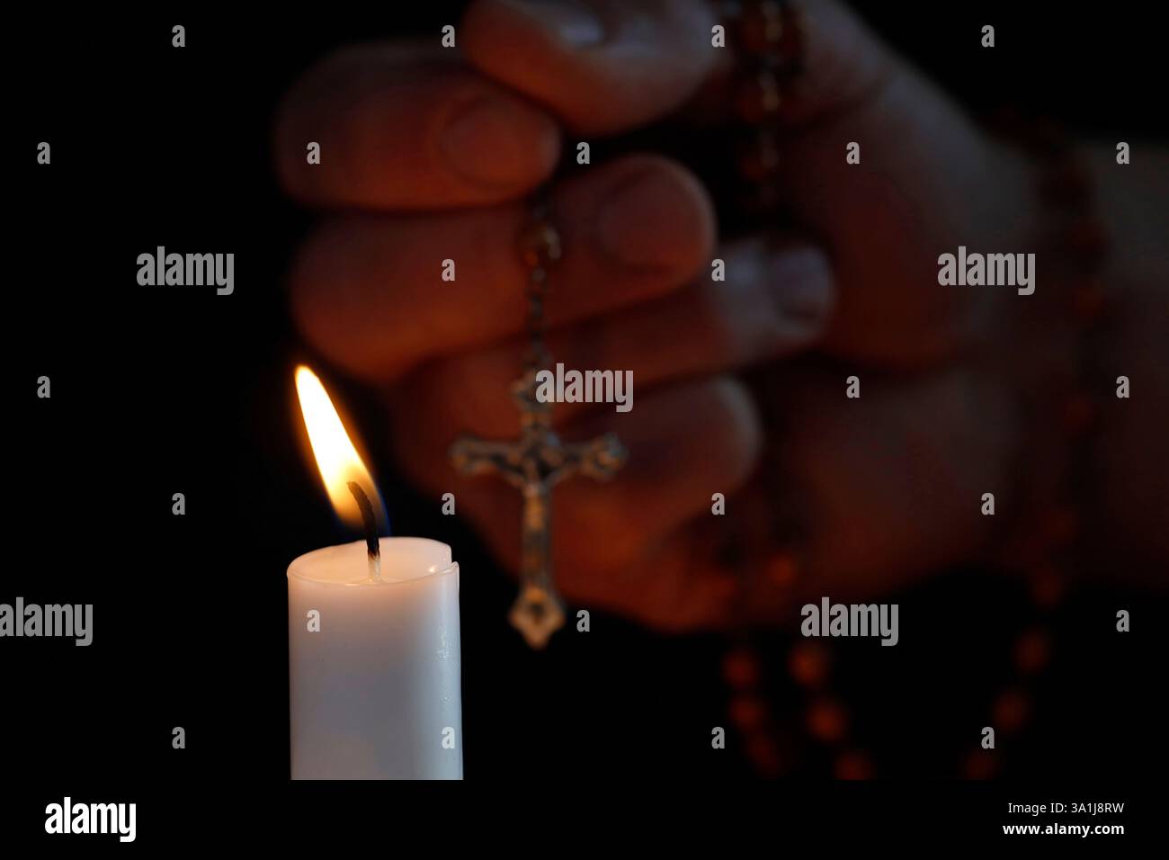 Burning white candle with rosary and praying hand on dark background ...
