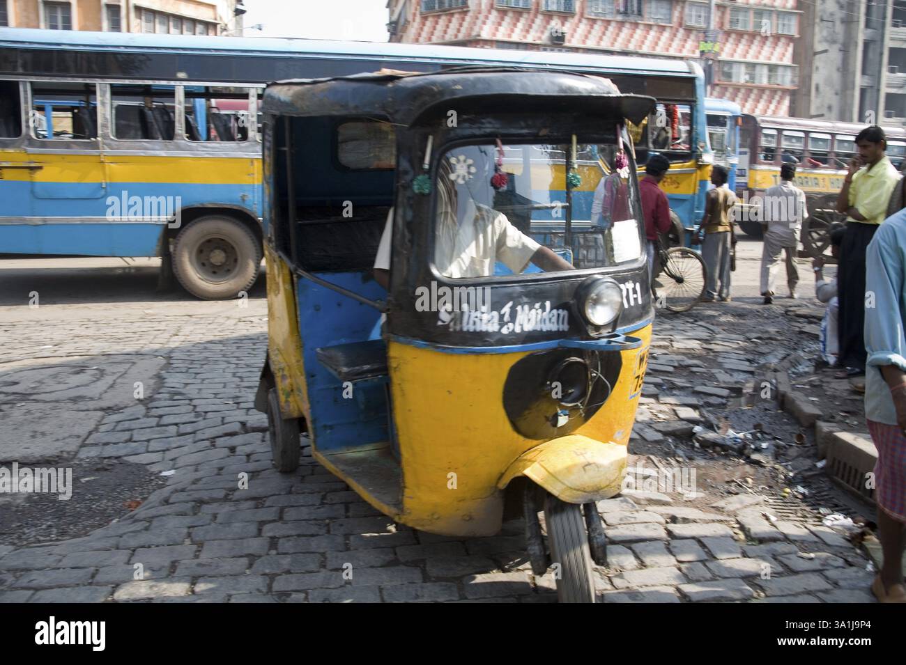 Yellow rickshaw and blue bus street scene near Howrah railway station ...