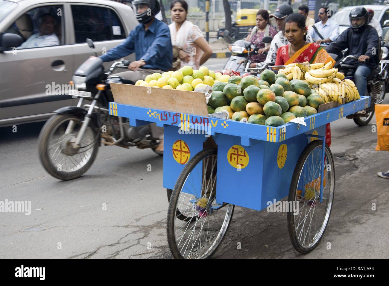Indian woman selling fruits on blue three wheeler cart traffic on road ...