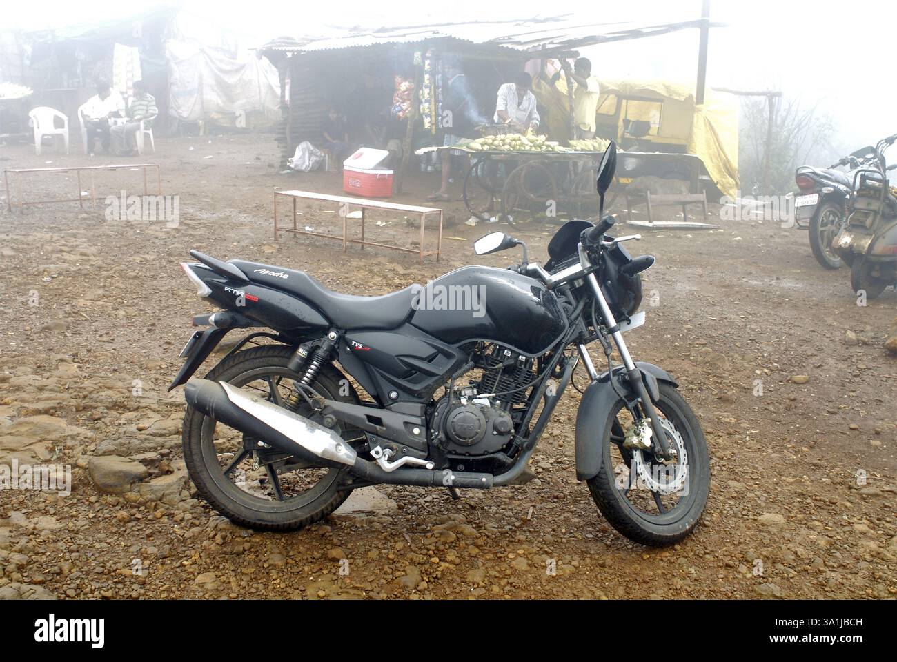 A two wheeler motor cycle parked near a stall selling corn on a foggy ...