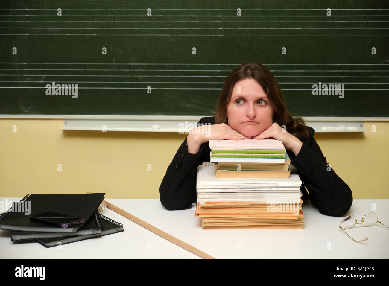 A worried female professor sitting by the chalkboard, her face showing ...