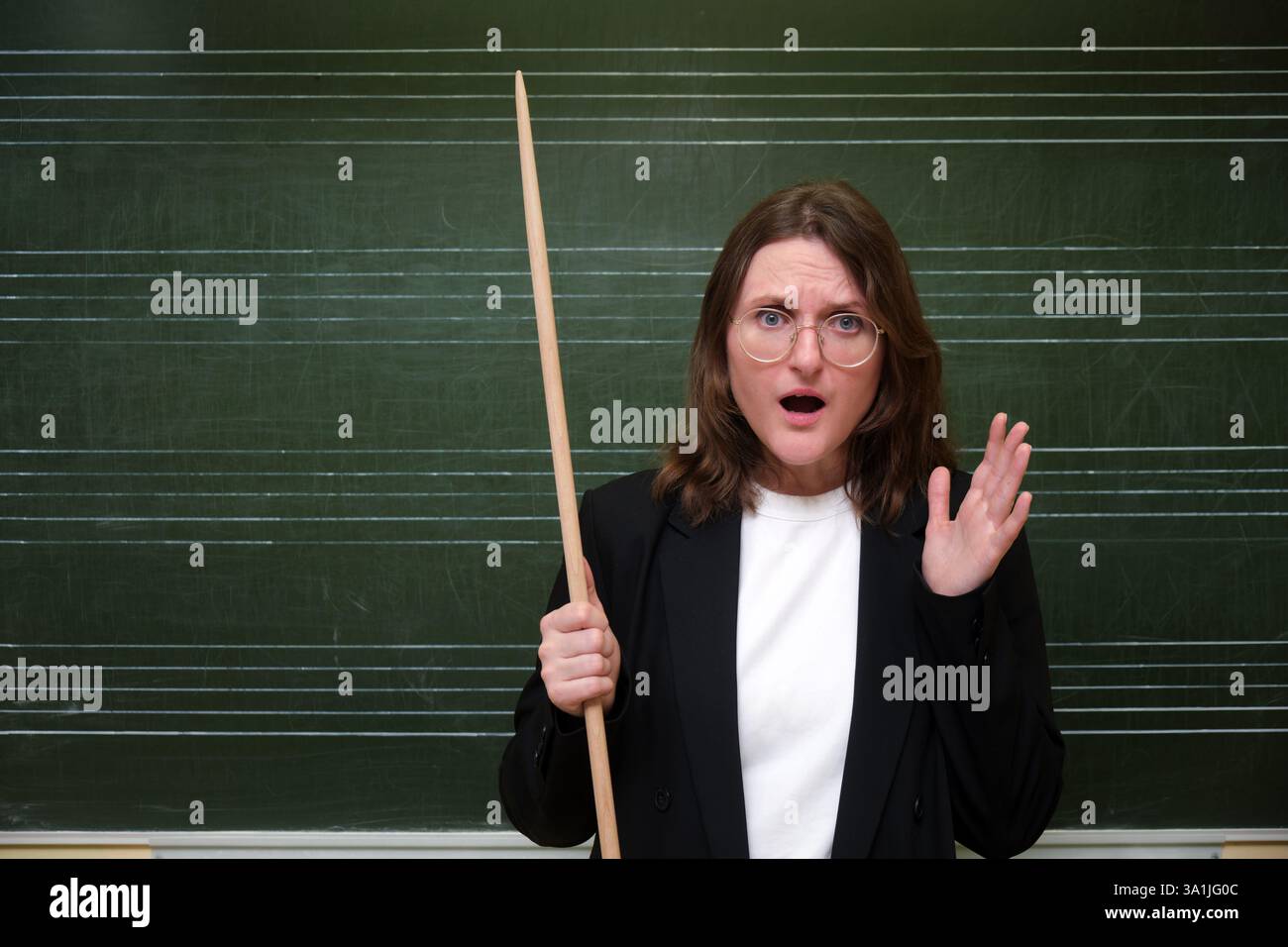 The female teacher, standing by the blackboard with a pointer, looks in ...