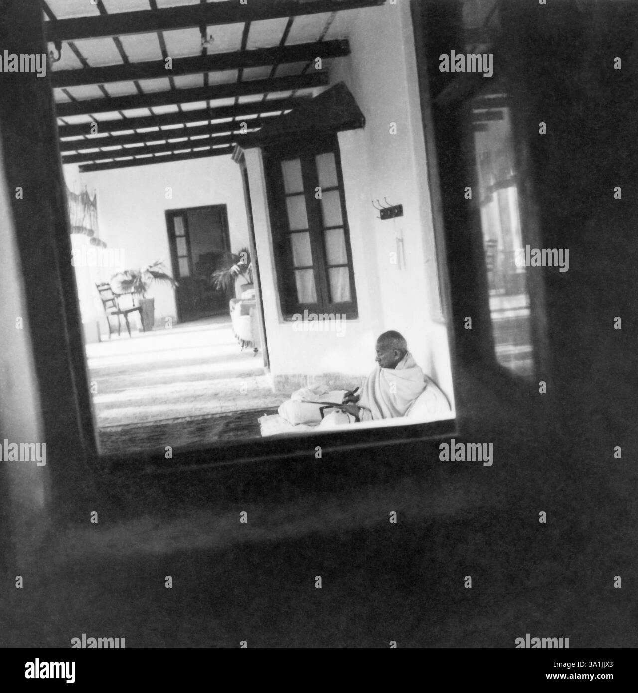 Mahatma Gandhi, seen through a window, writing during his visit to the ...