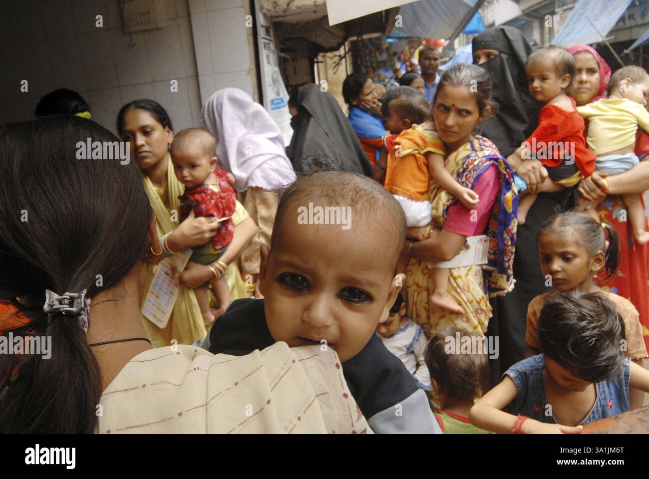 Muslim women stand in a queue with their children at a pulse polio ...
