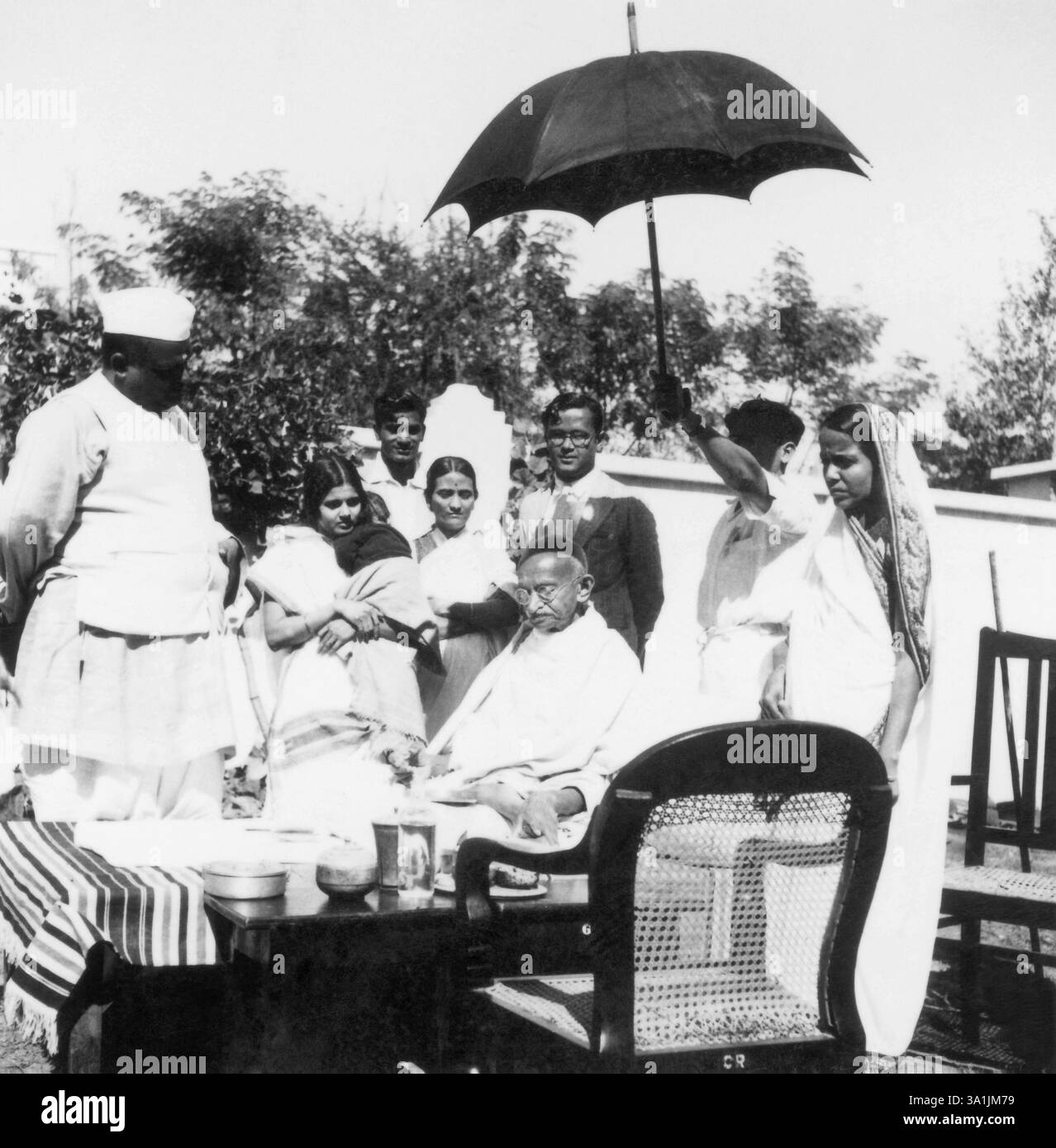 Mahatma Gandhi, sitting on a table, surrounded by people at Benares ...