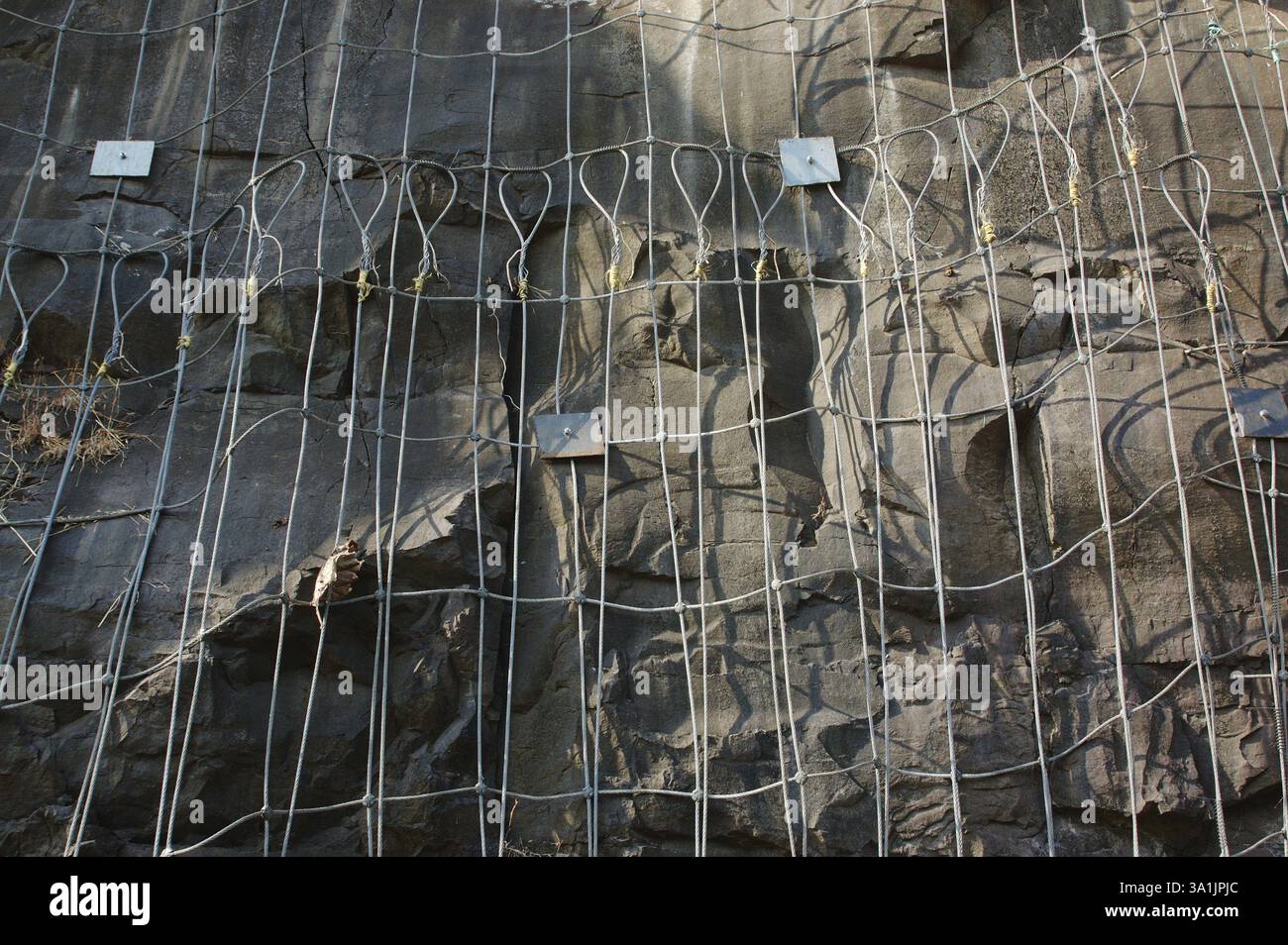 Net of steel wire nailed in rocks to hold loose rocks of the steep cut ...