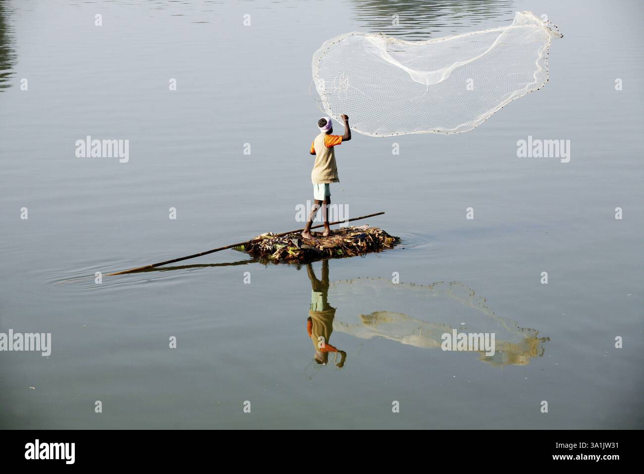 A fisherman from the Haripur village on a makeshift boat throwing his ...