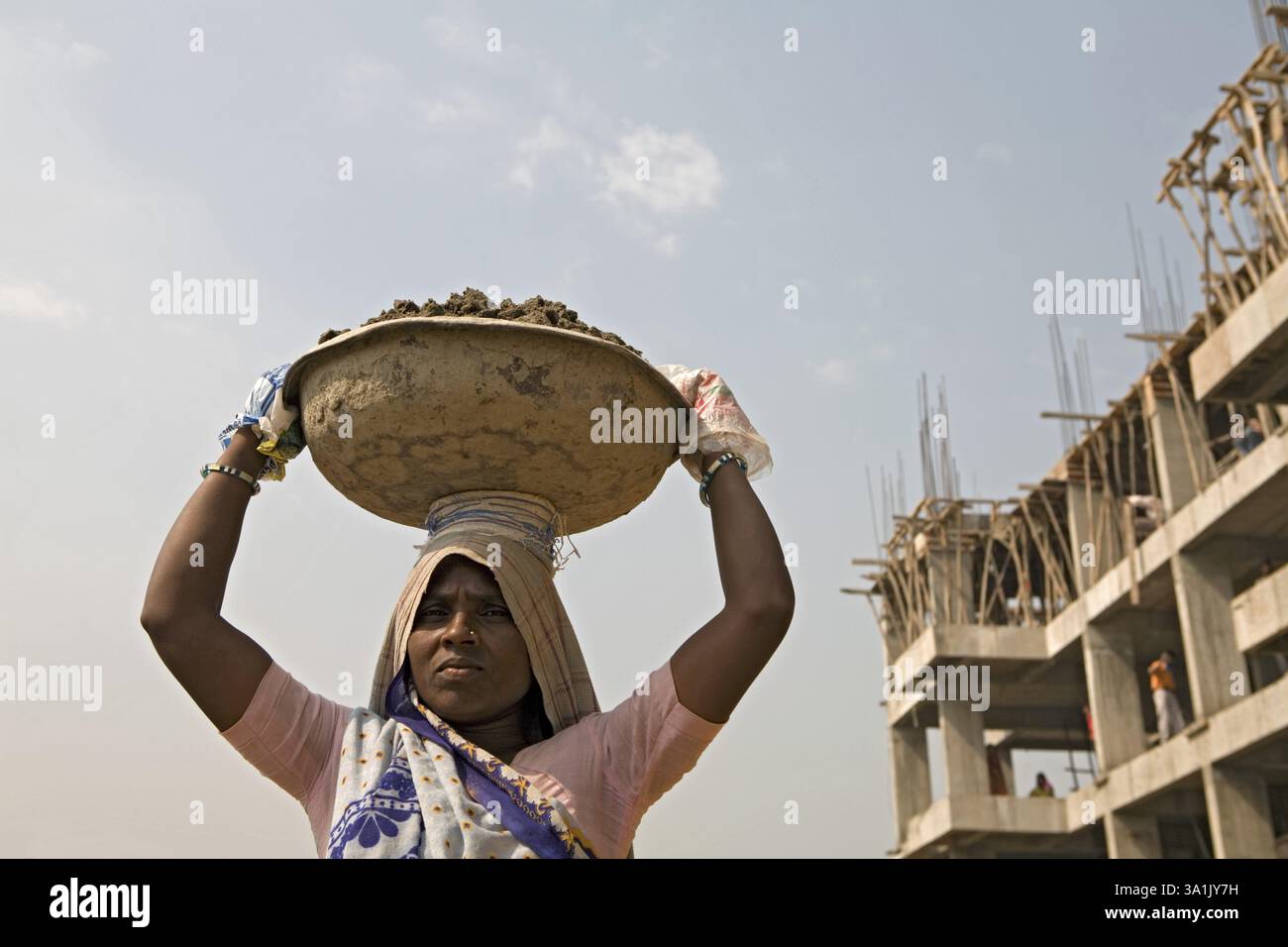 A woman carrying a load of cement mix on her head with her hands ...