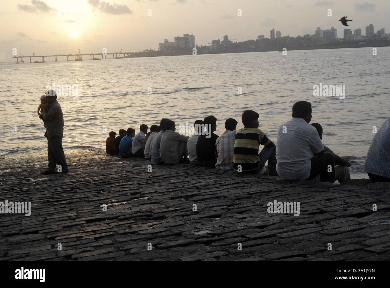 People sit in line enjoying cool sea breeze at Mahim beach on Arabian ...