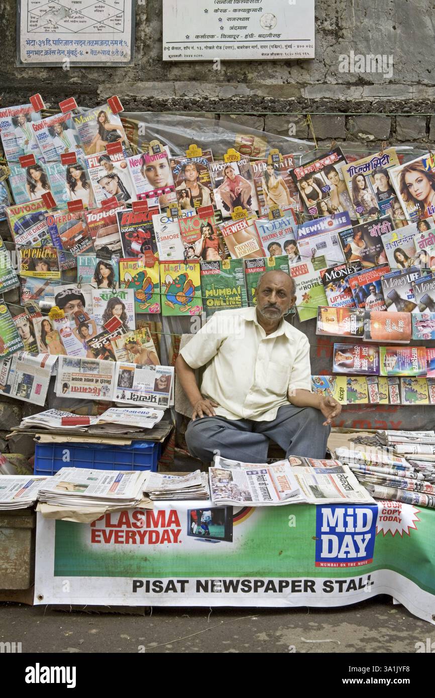 A newspaper vendor amidst his display of newspapers and magazines on ...