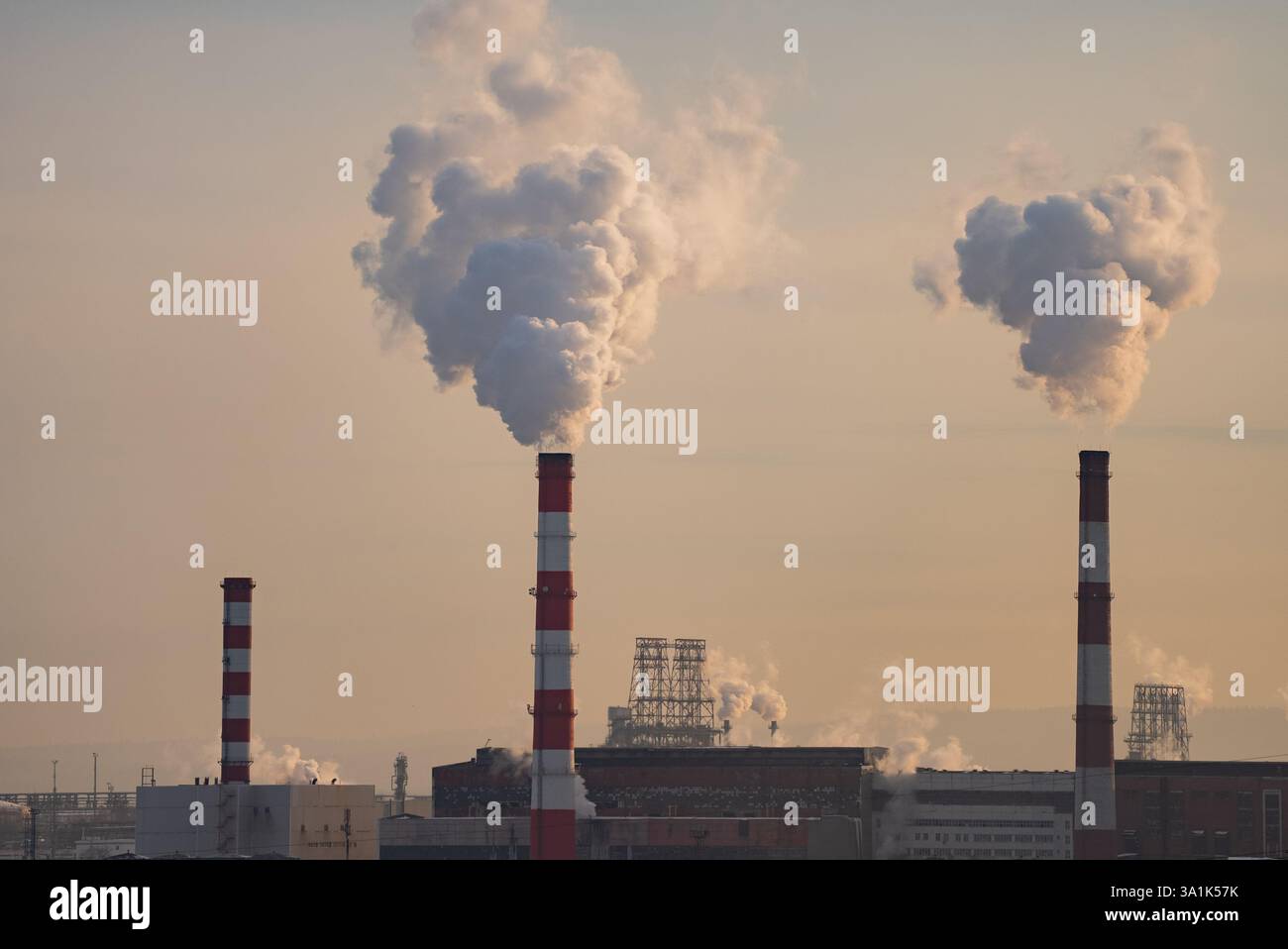 Smoke billowing from industrial chimneys against a vibrant sunset sky ...