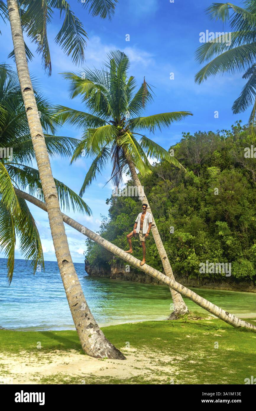 Young man standing on leaning palm trees on a beautiful tropical beach ...