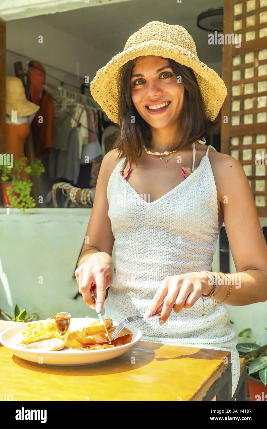 Young woman wearing a straw hat enjoying a delicious breakfast at an ...