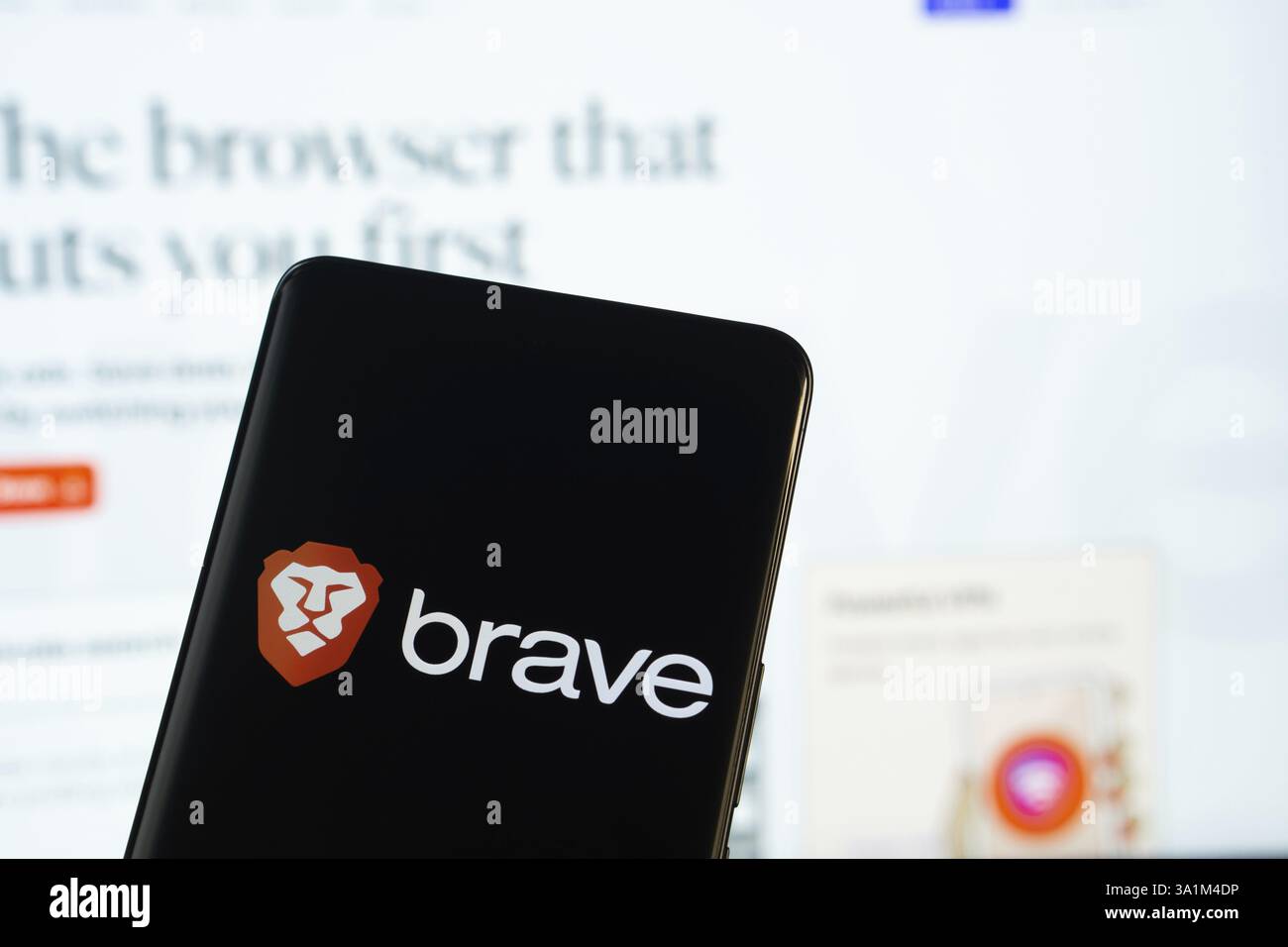 Brave logo is displayed on a smartphone screen, with the brave website visible on a computer ...