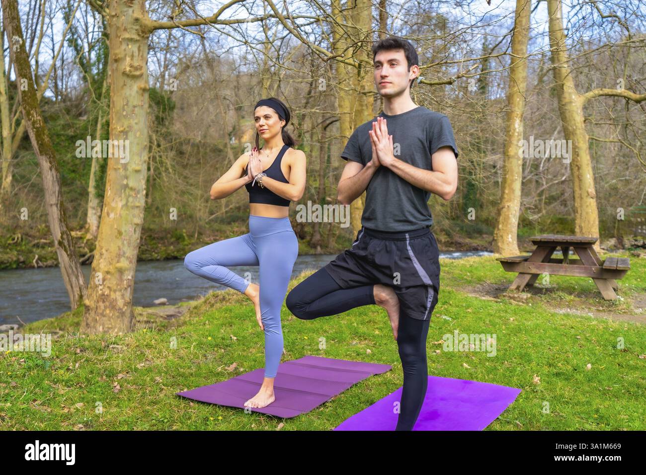 Yoga instructors performing the tree pose by a river in a forest ...