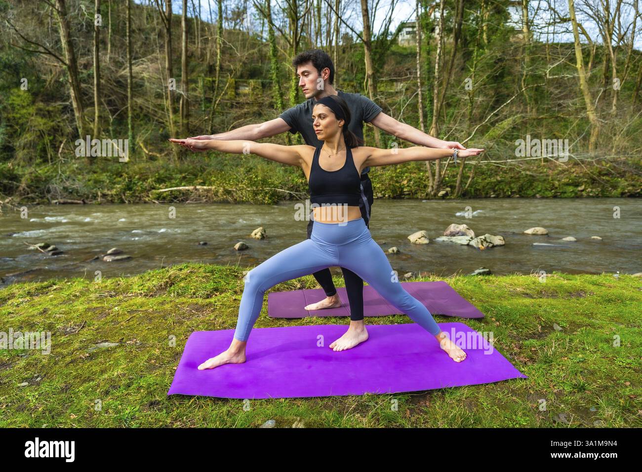 Yoga instructors performing virabhadrasana ii pose by a river ...