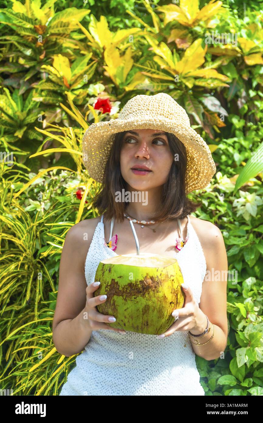 Young woman wearing straw hat holding fresh coconut water in tropical ...