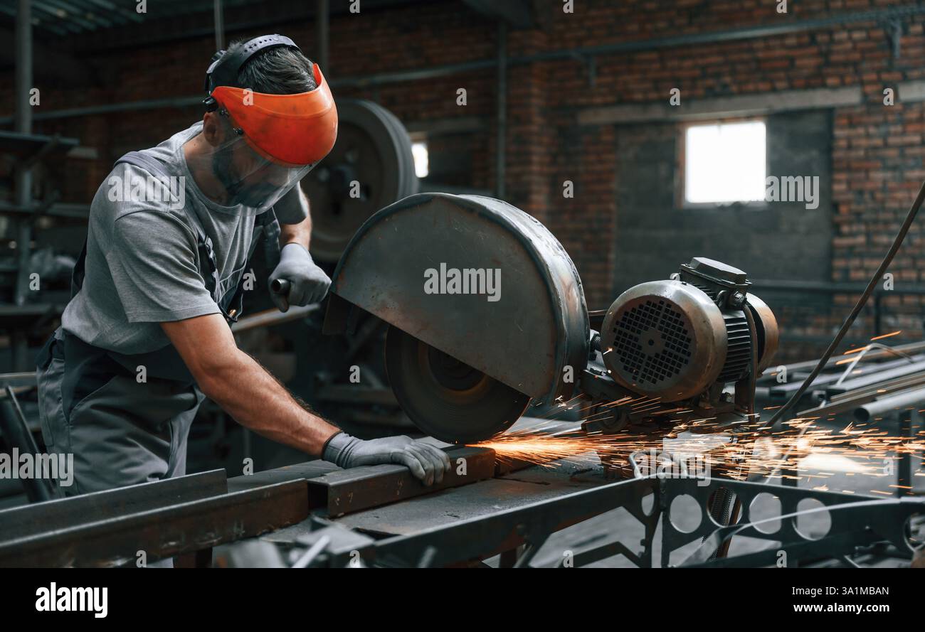 Process of cutting the metal. Young factory worker in grey uniform ...