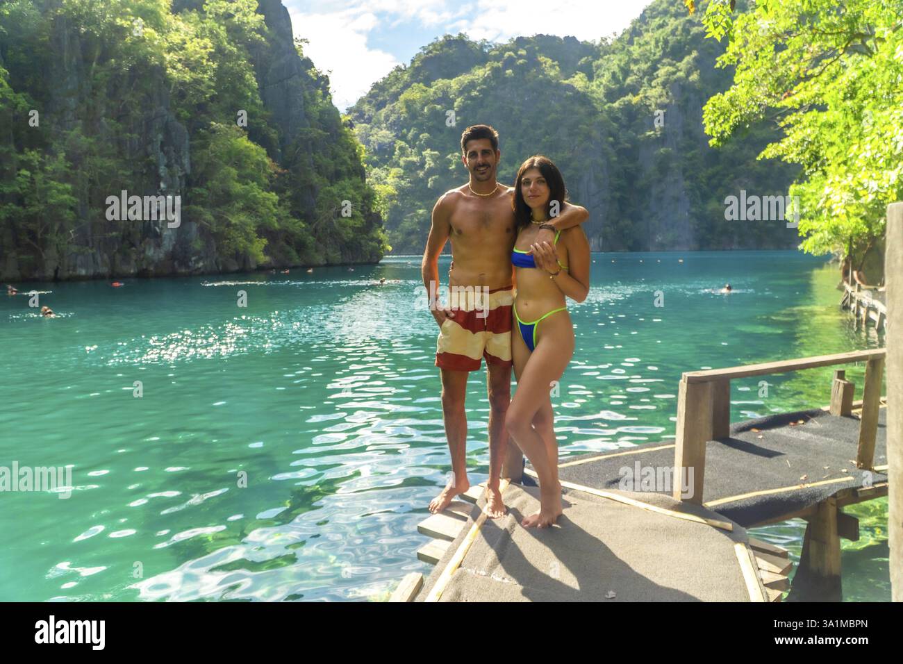 Couple standing on a wooden pier enjoying the turquoise water of kayangan lake, a popular ...